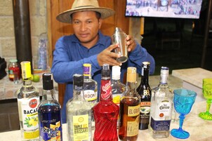 Um bartender segurando um coqueteleira com diversas garrafas de álcool e copos sobre o balcão.