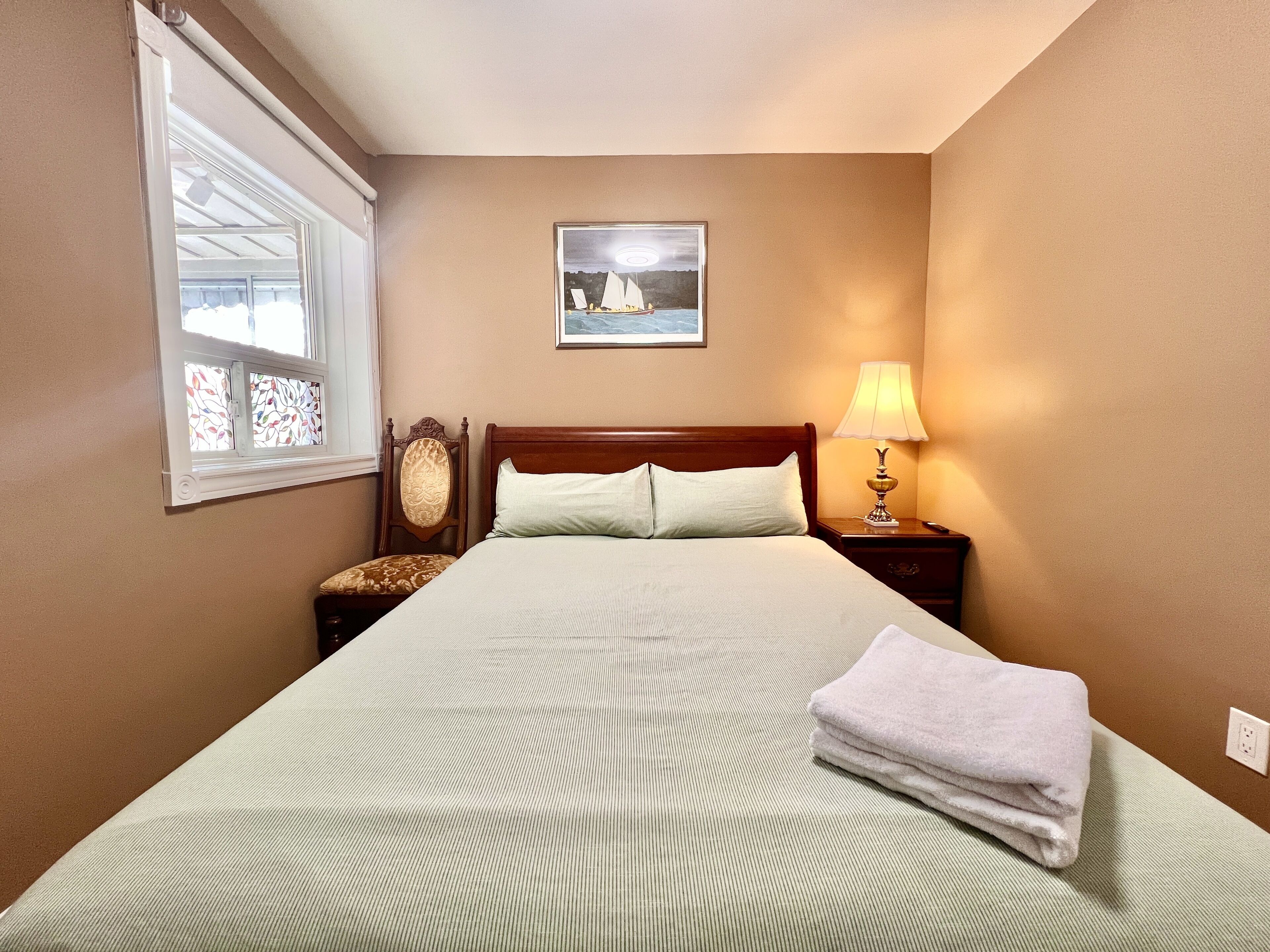 Cama bem arrumada com toalha dobrada, luminária de cabeceira e quadro na parede.