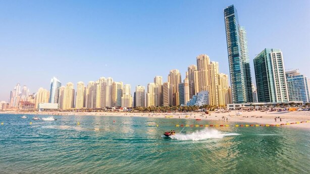 Paisagem costeira com edifícios altos, uma praia e um jet ski na água.