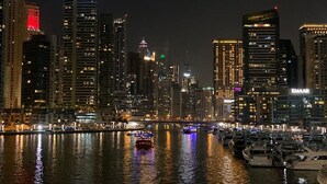 Paisagem urbana noturna com edifícios iluminados e um porto com barcos.