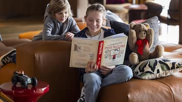 Duas crianças sentadas num sofá de couro marrom, lendo um livro intitulado 'Le Grand Livre de Petit Nicolas'.