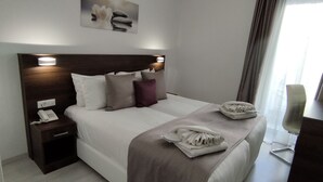 Quarto de hotel moderno com uma cama bem arrumada, telefone ao lado da cama, abajur e um quadro na parede.