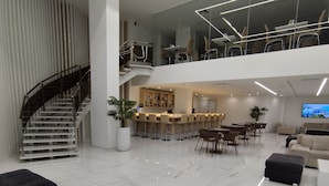 Um hall amplo com teto alto, escadaria, área de bar e espaços para sentar.