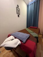 Sala de massagem com mesa de massagem, toalhas e relógio de parede.