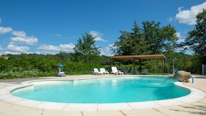 Piscina com deck de madeira e espreguiçadeiras, cercada por vegetação e árvores.