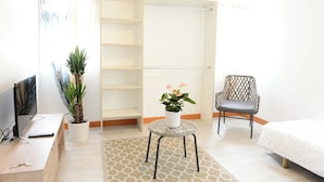 Quarto de hotel com cama, televisão, escrivaninha com planta, cadeira e guarda-roupa.