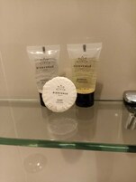Artigos de higiene em uma prateleira de vidro, incluindo um sabonete e duas garrafas de shampoo.