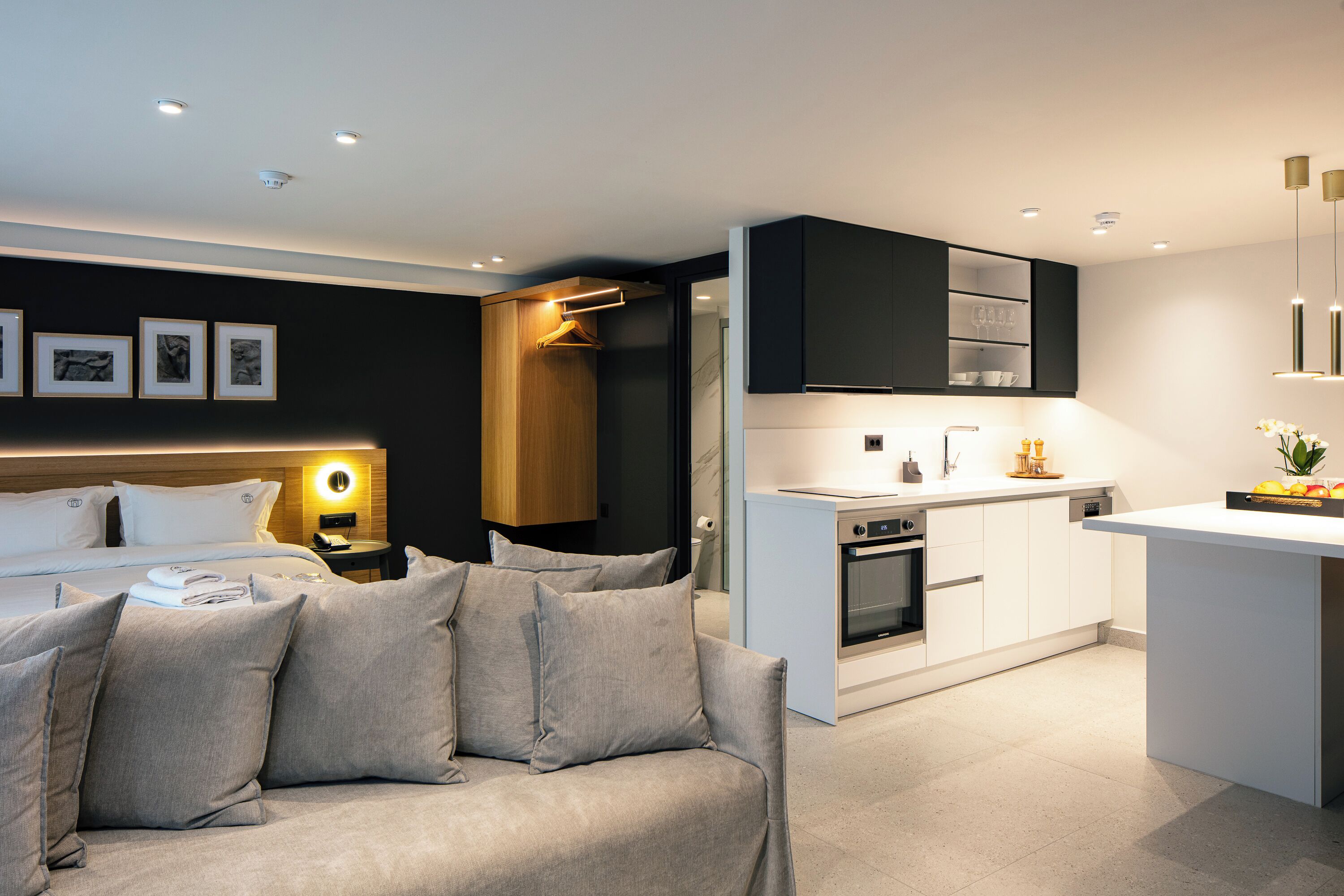 Quarto de hotel moderno com sofá, cama, cozinha compacta e banheiro.