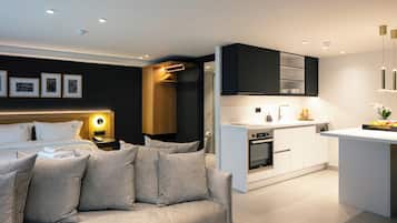 Quarto de hotel moderno com sofá, cama, cozinha compacta e banheiro.
