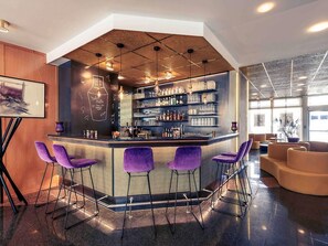 Uma área de bar com um balcão central, banquetes roxos e prateleiras repletas de garrafas e copos.