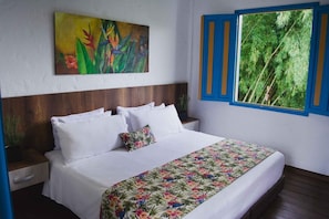 Uma cama com roupa de cama branca, um espalha-cama estampado com flores e um quadro acima.
