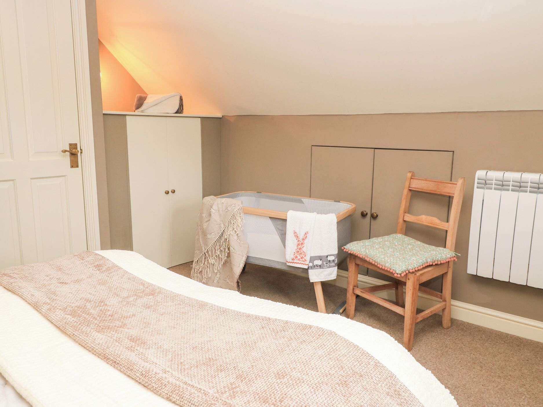 Quarto com cama, cadeira de madeira, escrivaninha com cadeira, radiador e guarda-roupa.