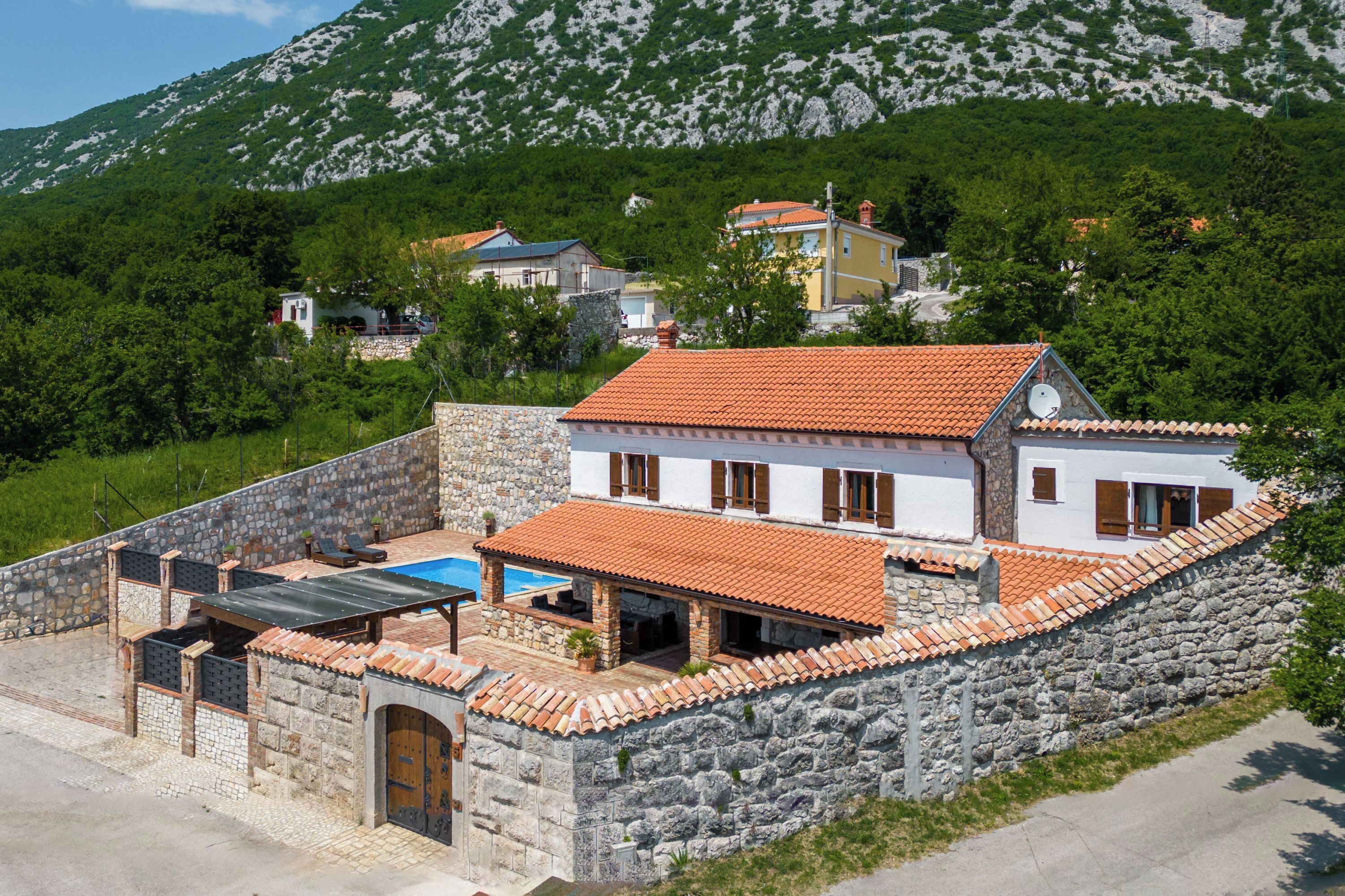 Uma casa de paredes de pedra com telhado ladrilhado, piscina e escadaria de pedra que leva à entrada.
