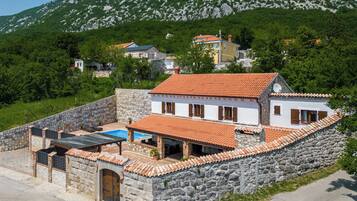 Uma casa de paredes de pedra com telhado ladrilhado, piscina e escadaria de pedra que leva à entrada.
