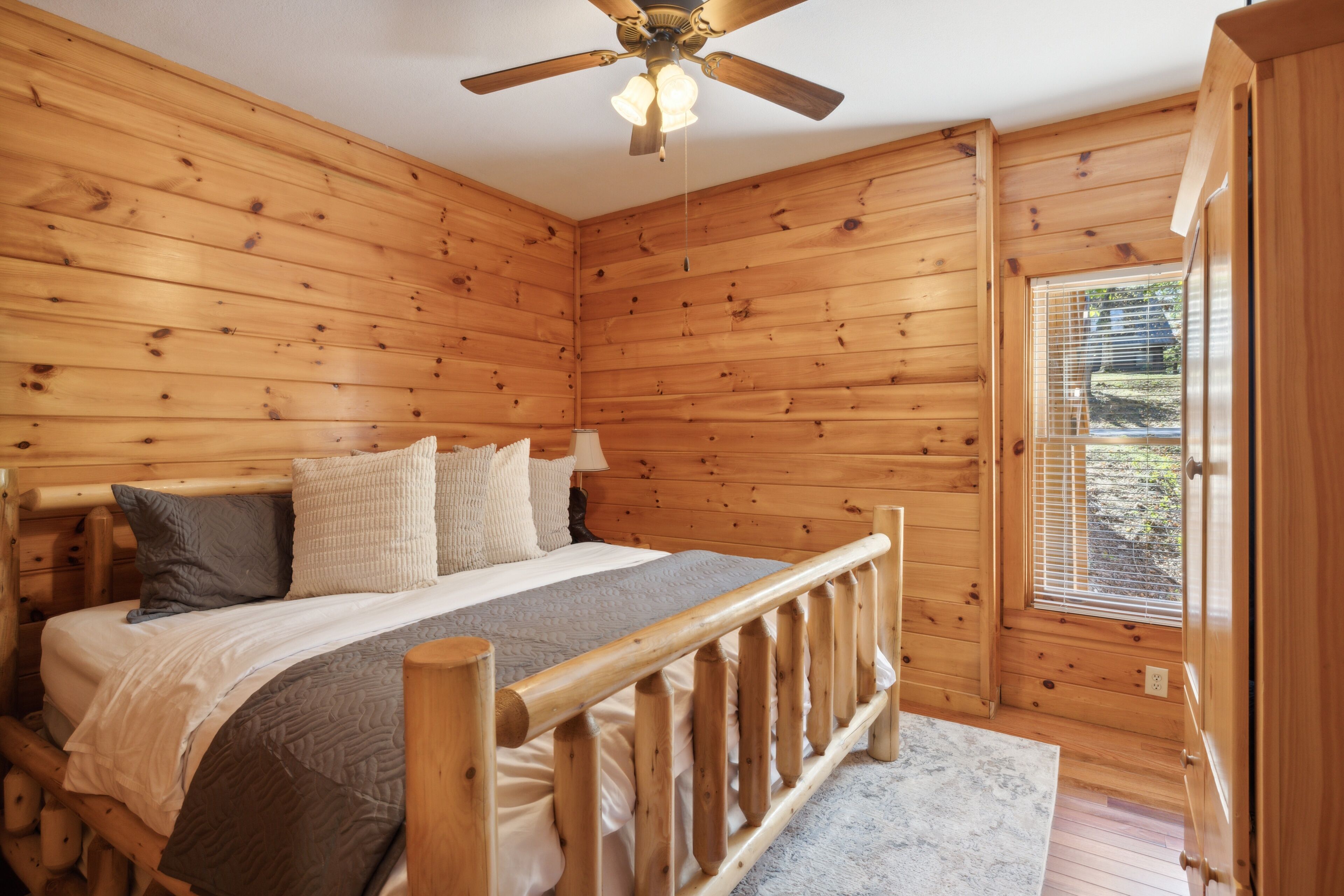 Quarto com painéis de madeira, cama, ventilador de teto e janela com persianas.