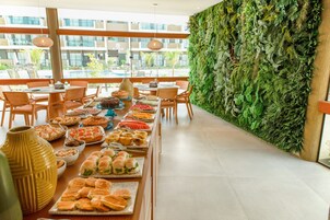 Disposição de buffet com diversos alimentos e um vaso grande sobre uma mesa.