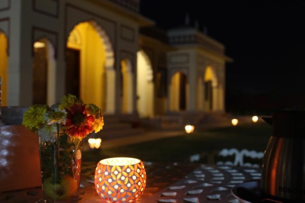Cena noturna com um candeeiro decorativo e um vaso de flores sobre uma mesa, com um edifício ao fundo.