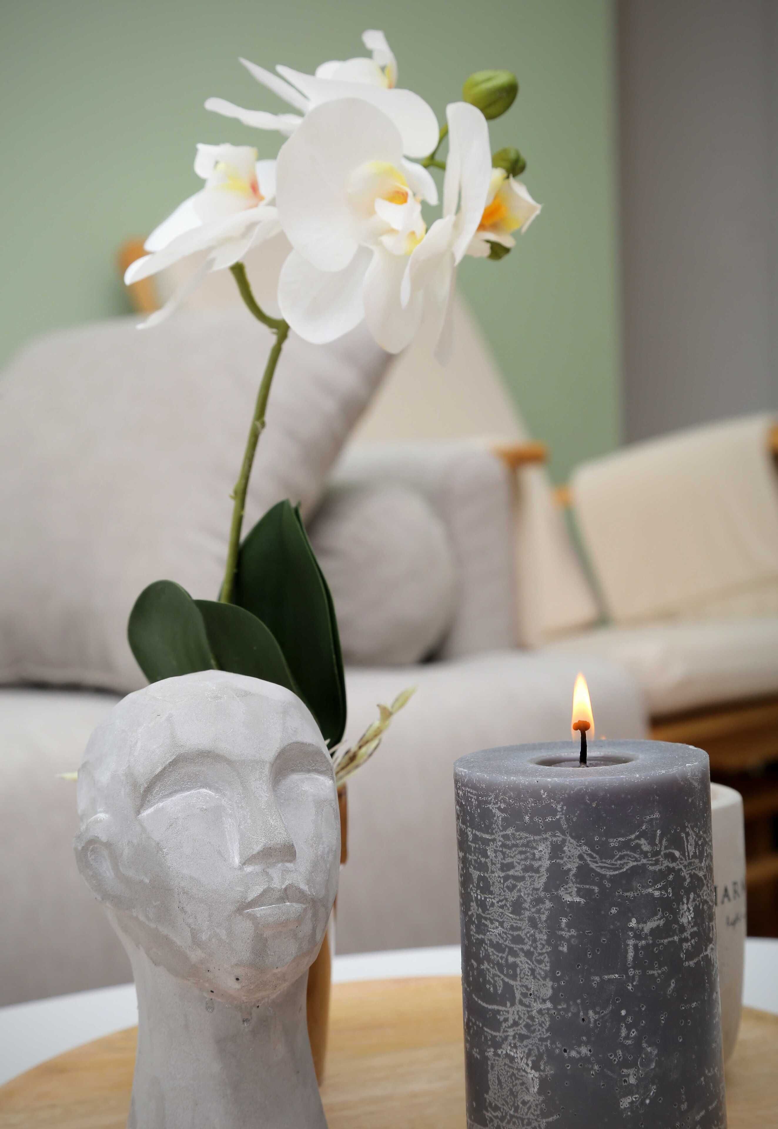 Um vaso de cerâmica branca com arranjo floral e uma vela acesa sobre uma mesa de madeira.