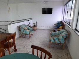 Quarto com mesa de jantar, cadeiras, televisão na parede e uma janela.