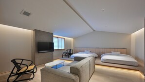 Quarto de hotel moderno com sofá, mesa pequena, televisão na parede e duas camas.