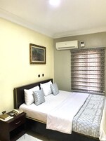 Quarto de hotel com cama, mesa de cabeceira e aparelho de ar condicionado.