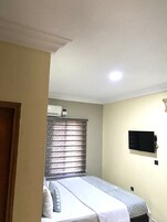 Quarto com cama, janela com cortinas, ar condicionado e televisão na parede.