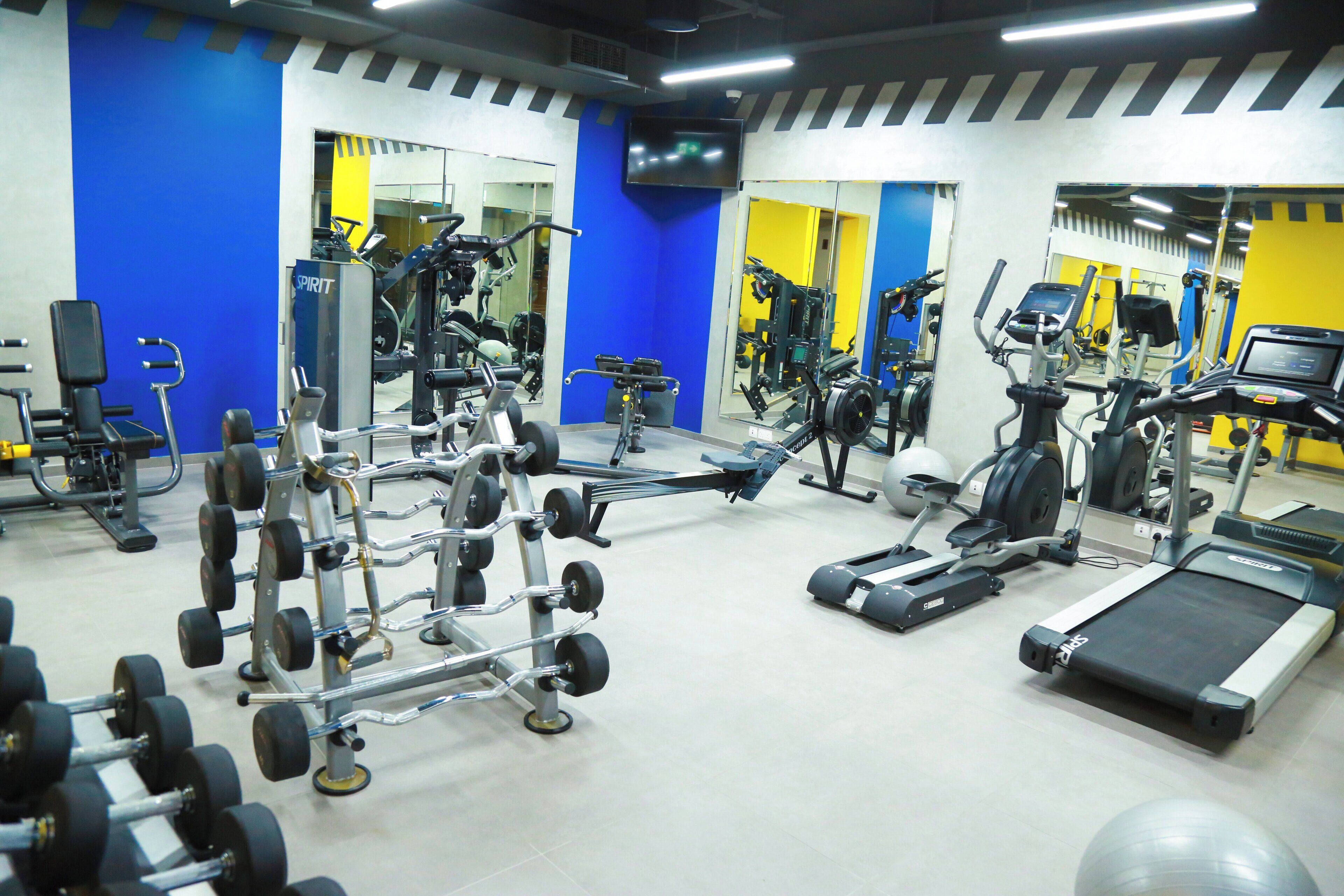 Uma academia com diversos equipamentos de exercício, incluindo esteiras, aparelhos de musculação e pesos livres.