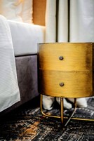 Uma cama com lençóis brancos, uma mesa de cabeceira dourada com duas gavetas e um tapete estampado.