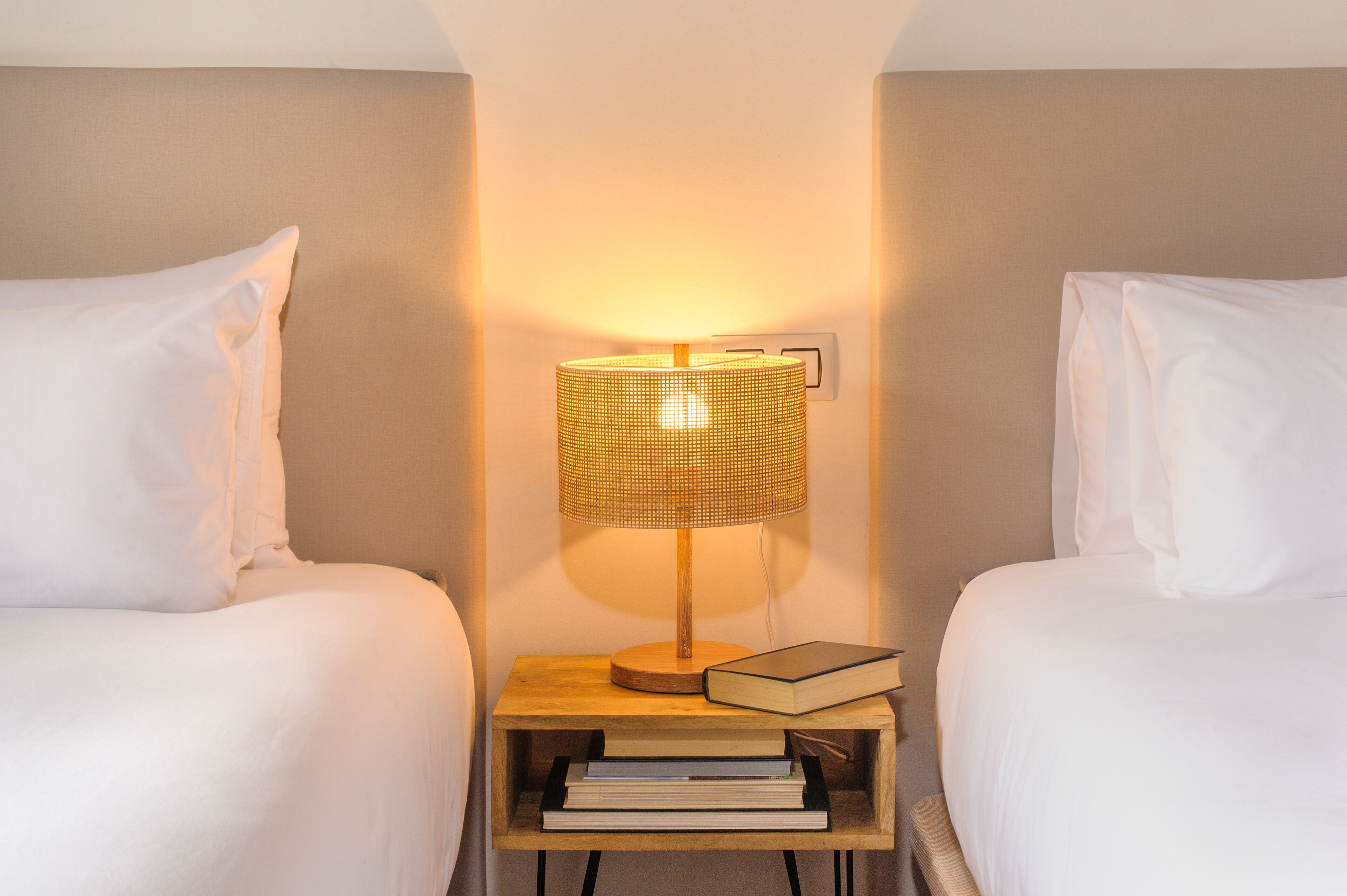 Quarto de hotel com duas camas, uma mesa de cabeceira com abajur e um livro.