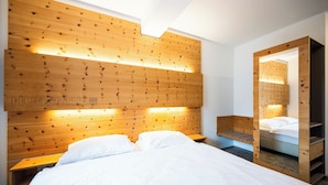 Um quarto com cabeceira de madeira, cama com roupa de cama branca, mesa de cabeceira e um espelho.