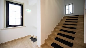 Uma escada com degraus de madeira e soleiras pretas, uma porta com janela e uma pequena placa de saída.