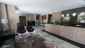 Uma área de recepção moderna com balcão, duas cadeiras roxas, balcão de madeira, piso de mármore e uma janela grande.