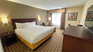Quarto de hotel com uma cama grande, uma escrivaninha, uma cadeira e uma mesinha.
