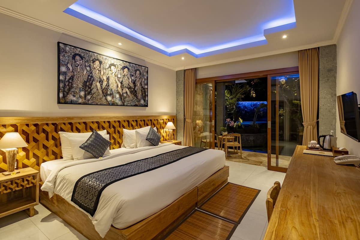 Quarto de hotel moderno com uma cama grande, cabeceira de madeira e um quadro acima. Há uma varanda com porta de vidro e vista para o exterior.
