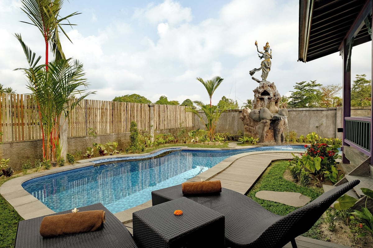 Piscina com deck de madeira, espreguiçadeiras e uma estátua.