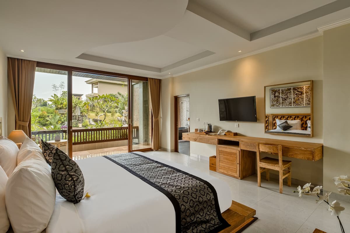 Quarto de hotel com cama grande, escrivaninha, TV de tela plana e varanda com vista para área verde.