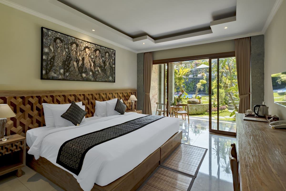 Um quarto espaçoso com uma cama grande, uma cabeceira de madeira, um quadro acima da cama e vista para um jardim através de uma porta de vidro deslizante.