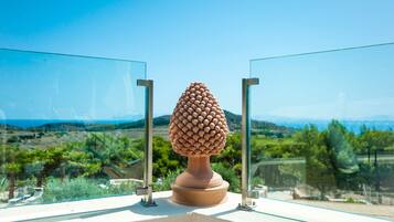 Escultura em terracota em uma varanda com grades de vidro, com vista para uma paisagem verde e colinas ao longe.