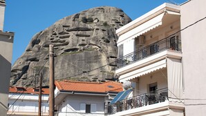 Um edifício com telhado de telhas vermelhas, uma varanda com grades pretas e uma grande formação rochosa ao fundo.