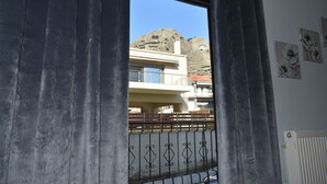 Vista pela janela com cortinas, mostrando um edifício com varanda e uma montanha ao fundo.