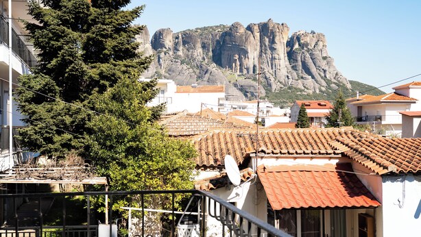 Área residencial com telhados vermelhos tradicionais, uma montanha rochosa imponente ao fundo e uma antena parabólica em uma casa.