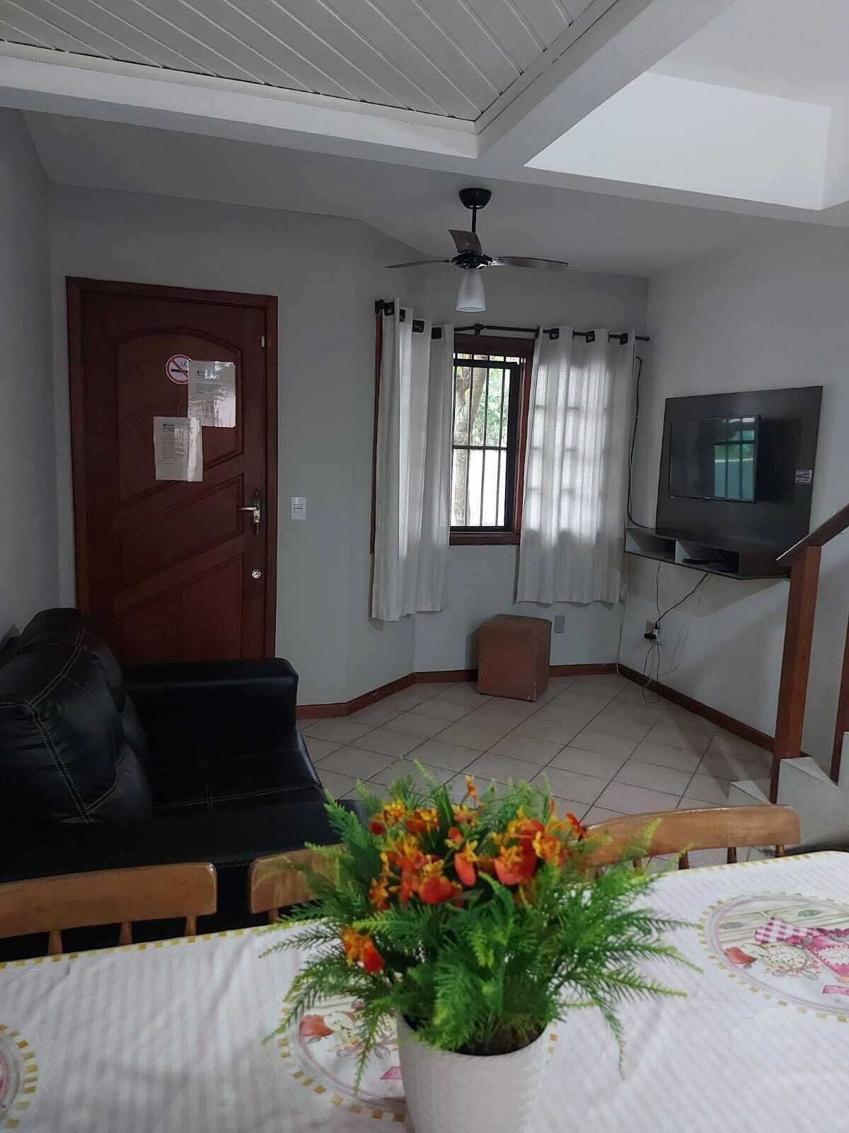 Quarto com cama, sofá, televisão, ventilador de teto e janela com cortinas.