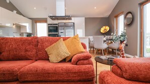Uma sala de estar moderna com um sofá vermelho, uma área de jantar com mesa e cadeiras, e uma cozinha ao fundo.