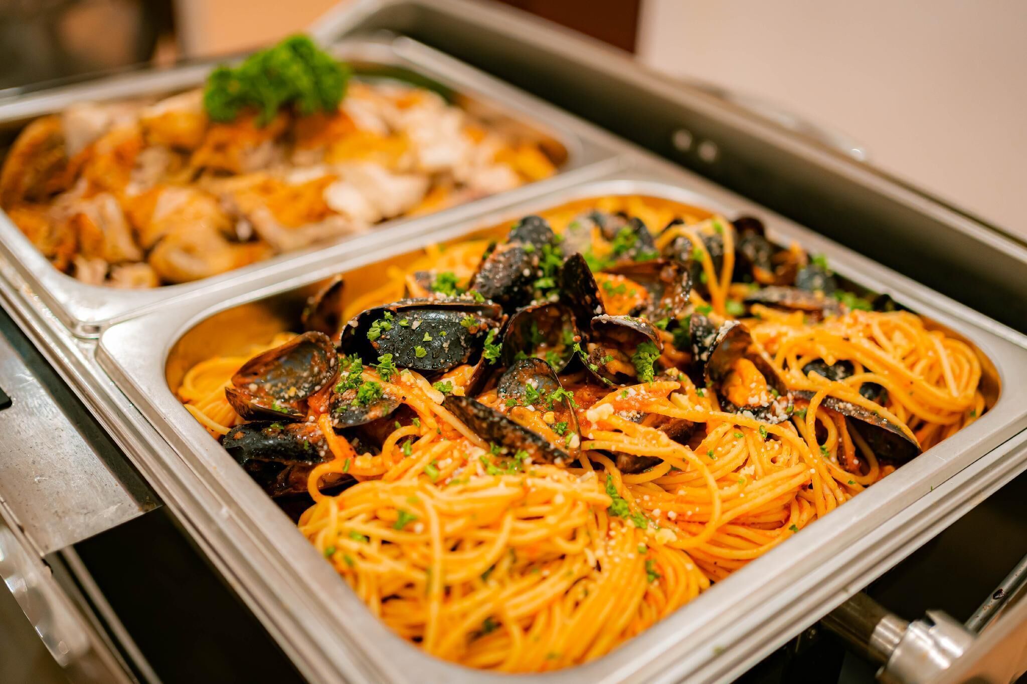 Buffet com pratos de massa, incluindo espaguete com mexilhões e frango.