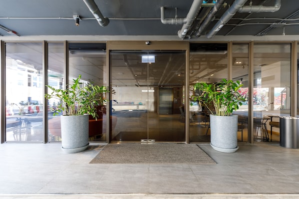 Uma entrada moderna com portas de vidro, duas grandes plantas em vasos e um chão de azulejos limpo.