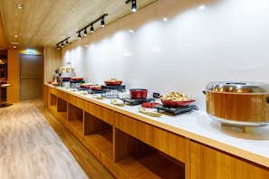 Um balcão de buffet extenso com diversos pratos e uma panela grande em cima de um fogão.