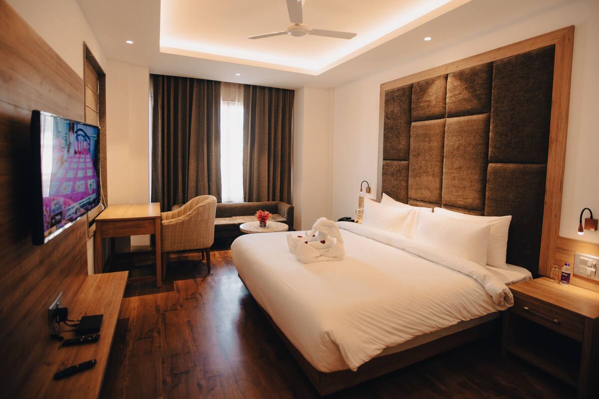 Quarto de hotel com cama, televisão, escrivaninha, cadeira e ventilador de teto.
