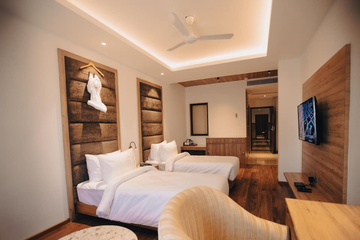 Quarto de hotel com duas camas, uma mesa redonda, uma cadeira, televisão e ventoinha no teto.