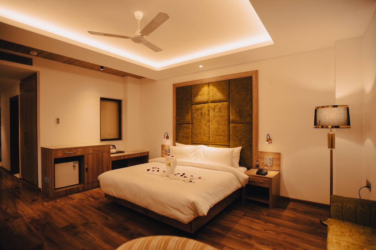 Quarto de hotel moderno com uma cama grande, um ventilador de teto, uma mesa de cabeceira com luminária e piso de madeira.