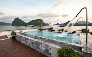 Uma piscina com um elemento aquático, rodeada por um deck de madeira e um muro de pedra.